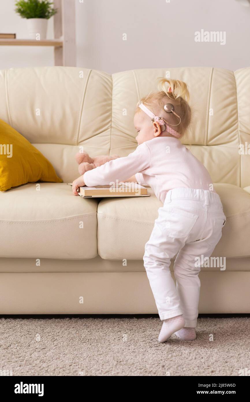 Lustiges Baby mit Cochlea-Implantat, das zu Hause sitzt und isst. Hören ...
