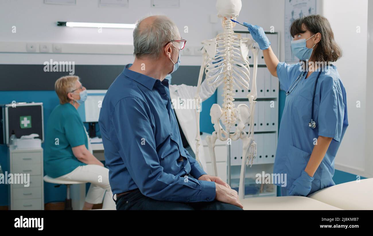 Weibliche Fachärztin, die auf das Rückenmark auf dem menschlichen Skelett zeigt, erklärt dem ...