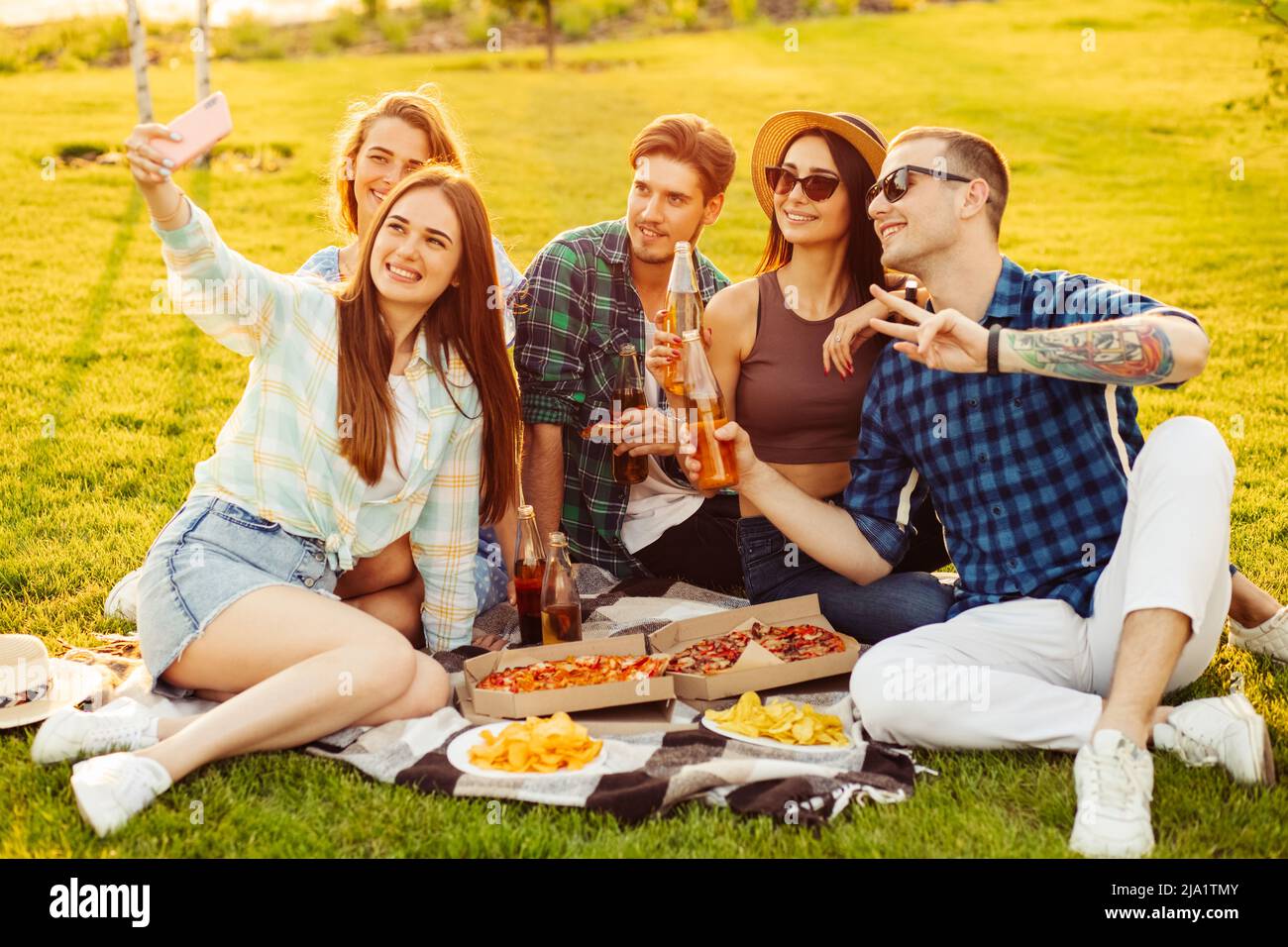 Glückliche Freunde machen ein Picknick im Stadtpark im Freien. Junge Leute trinken Getränke und ...
