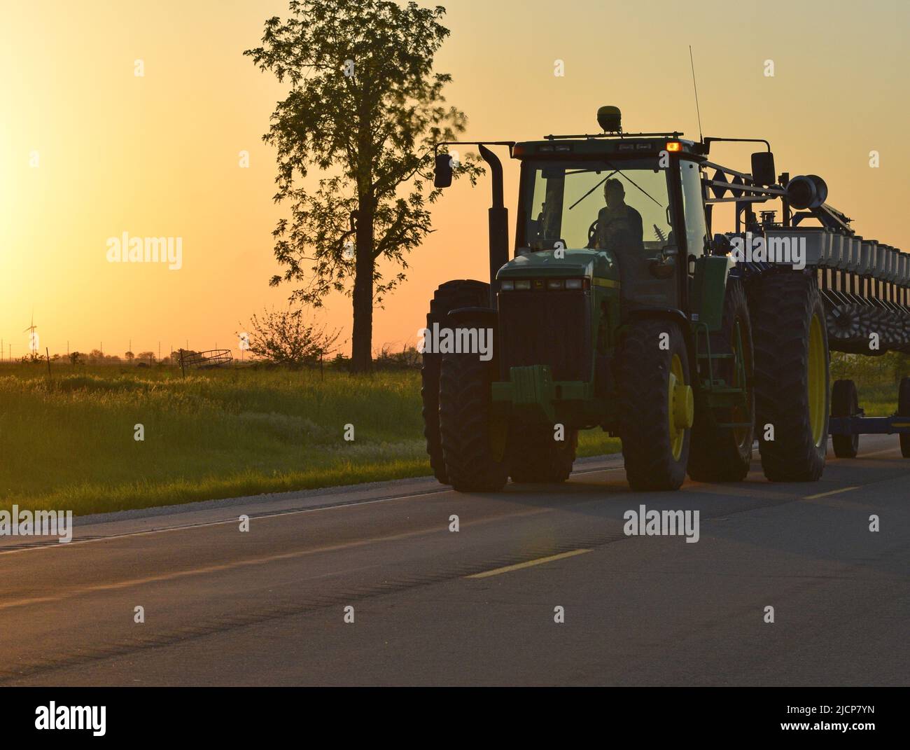 Ein großer John Deere-Traktor, der bei Sonnenaufgang auf dem US-Highway ...