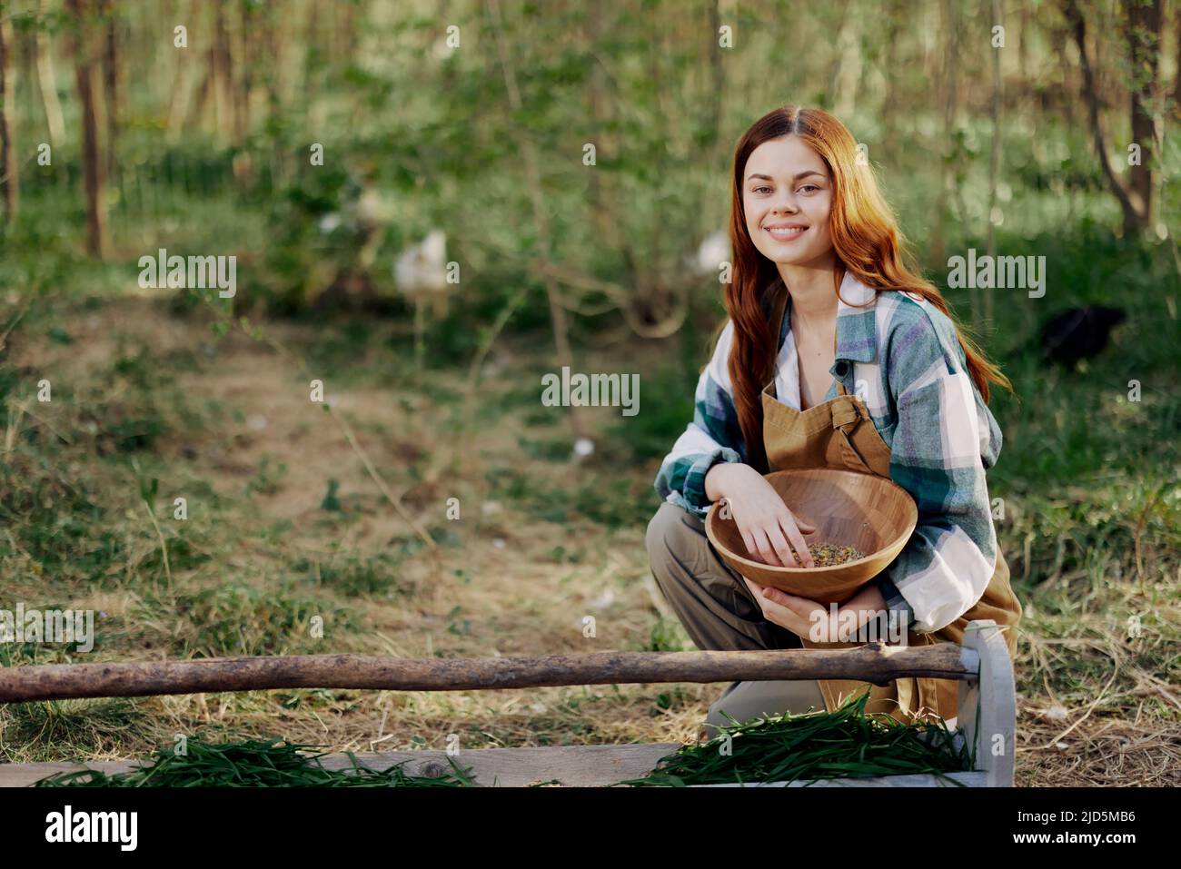 Eine Farmerin lächelt und gießt Futter für die Vögel aus einer Schüssel ...