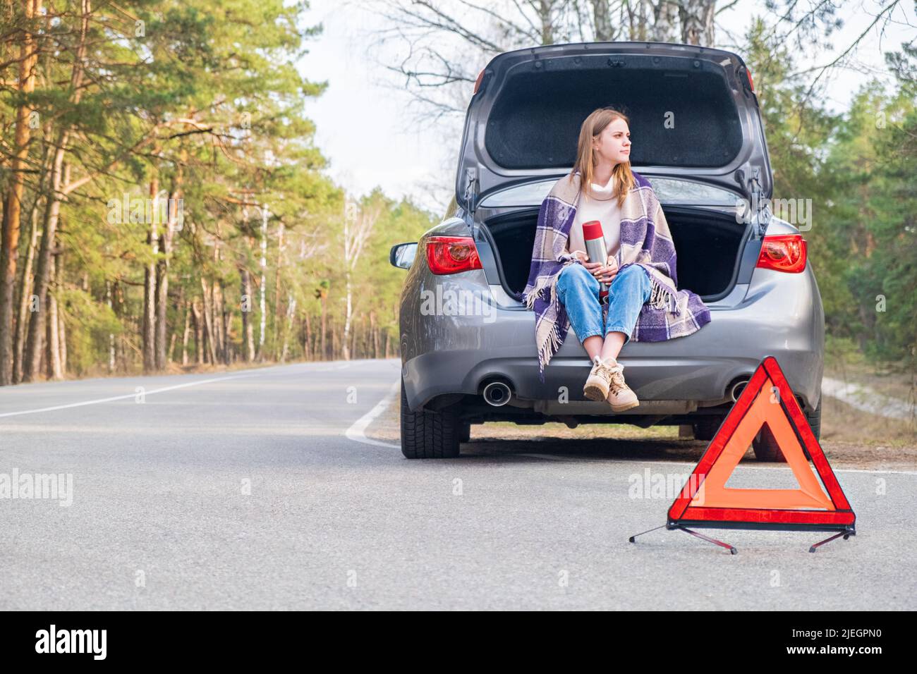 Rotes Notdreieck mit Auto und Frau, die im Kofferraum mit Thermoskannen ...