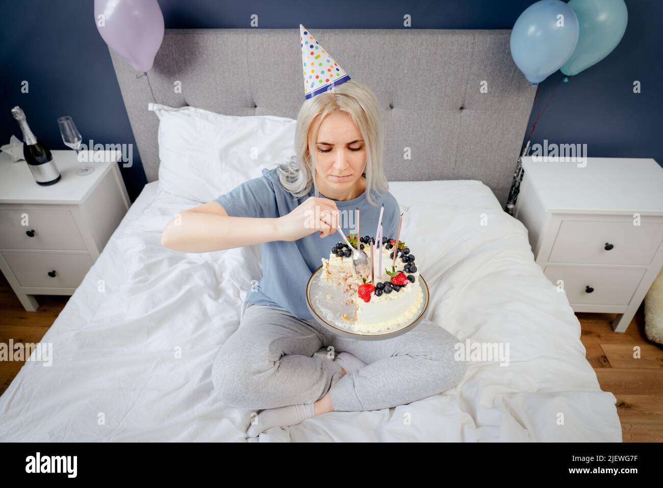 Traurige, verärgerte Frau in Pyjama und Partymütze, die mit Löffel ...