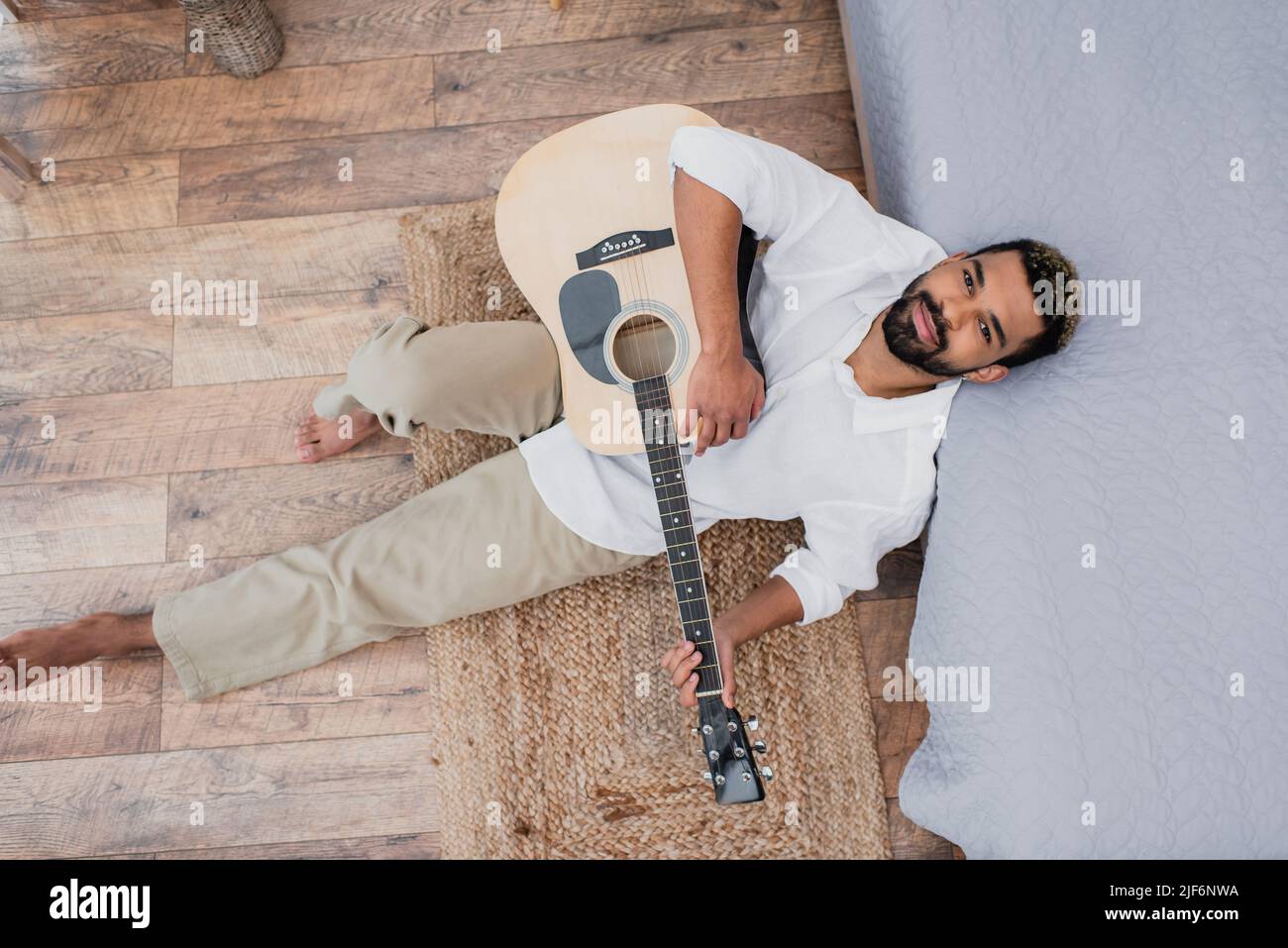 Draufsicht auf einen afroamerikanischen Mann mit gefärbten Haaren, die eine Akustikgitarre ...