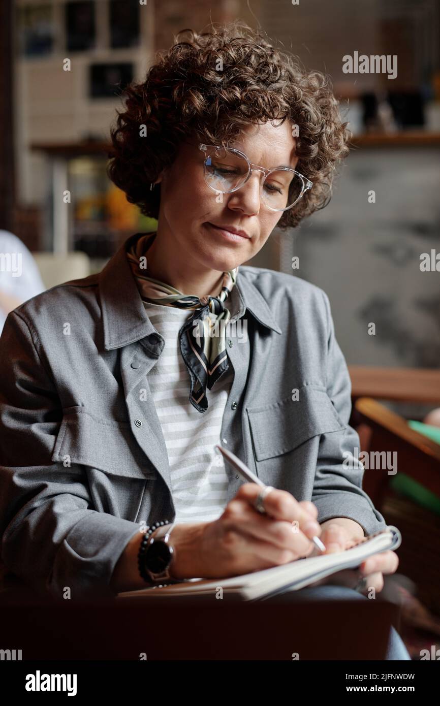 Junge seriöse Geschäftsfrau oder Freiberuflerin mit Stift über Copybook ...