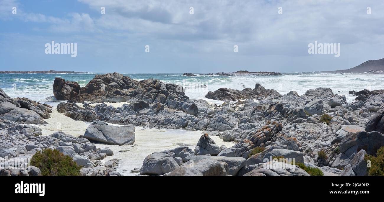 Eine felsige Küste an einem Strand in Kapstadt mit bewölkten Wolken ...