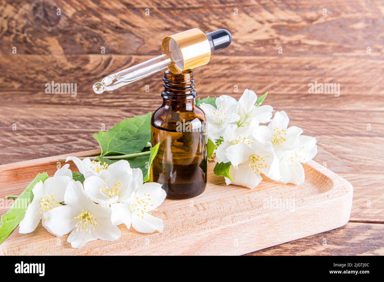 Eine offene Glasflasche mit Bio-Jasminöl steht auf einem Holztablett ...