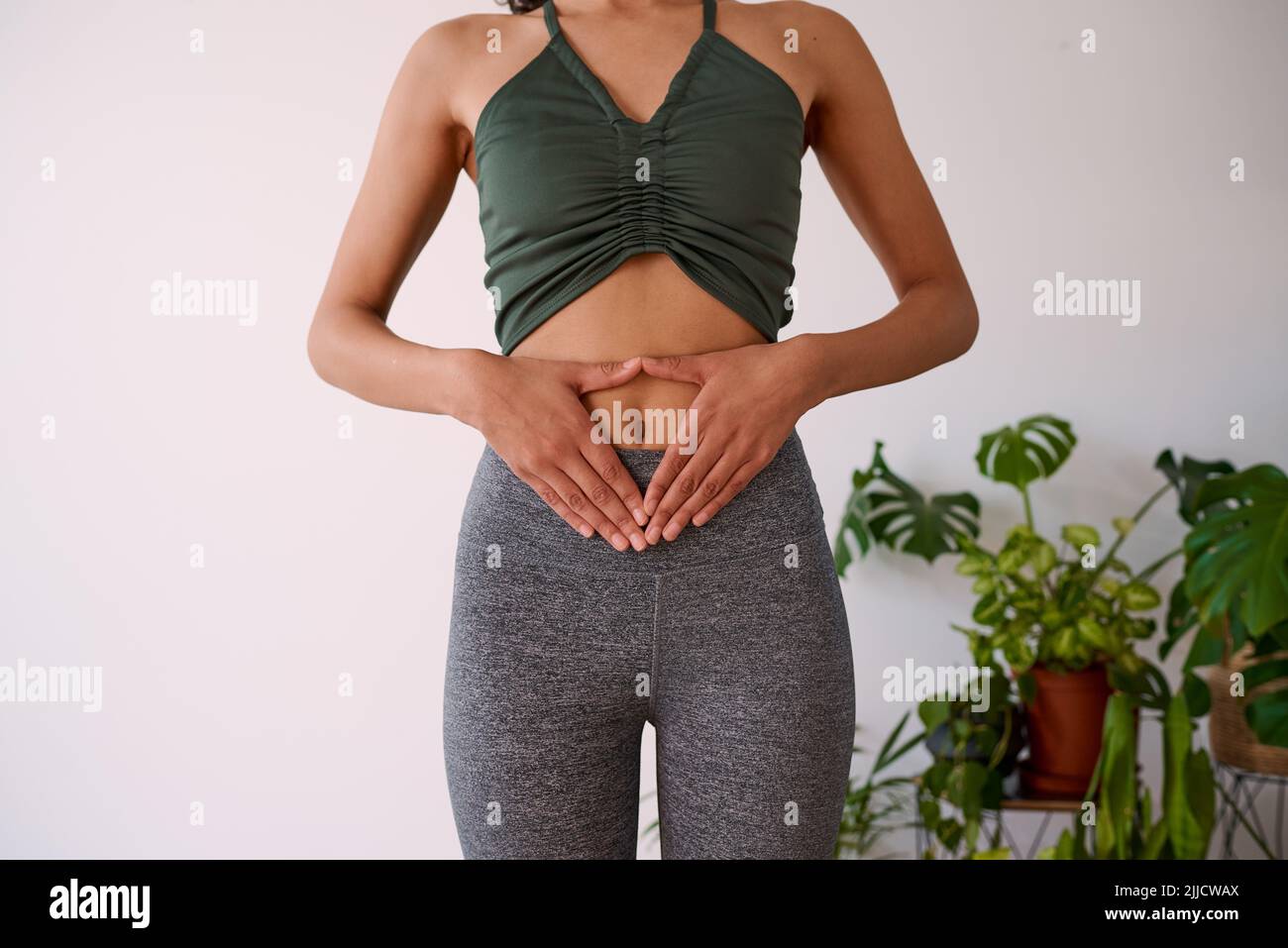 Eine junge, multiethnische Frau hält ihre Hände an ihrem Bauch, was die ...