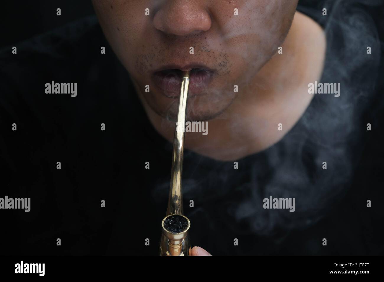 Ein asiatischer Mann raucht zu Hause aus einer Pfeife Marihuana. Studio ...