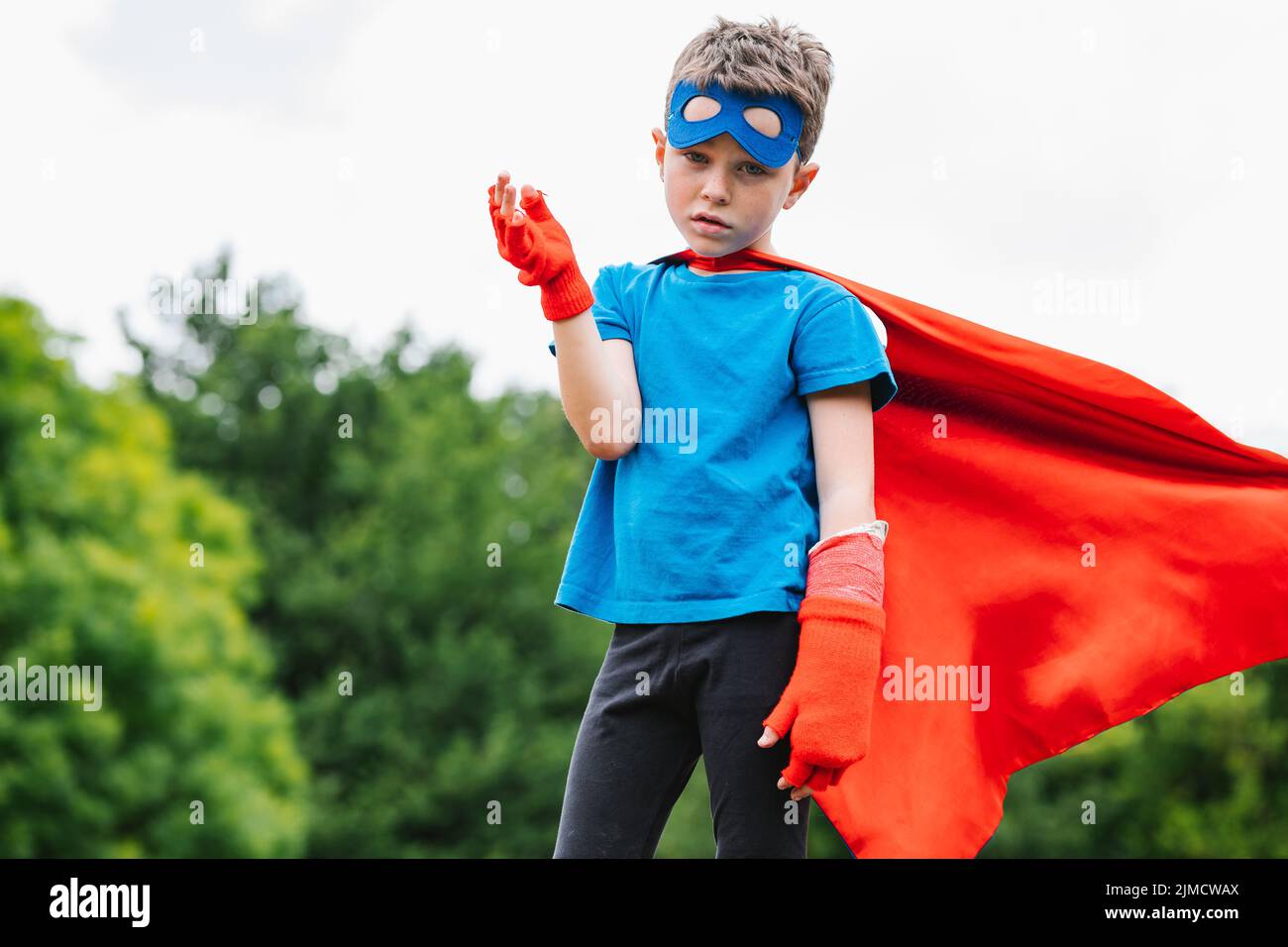 Kleiner Superheld mit Umhang und Maske, die den Arm hebt und die Kamera ...