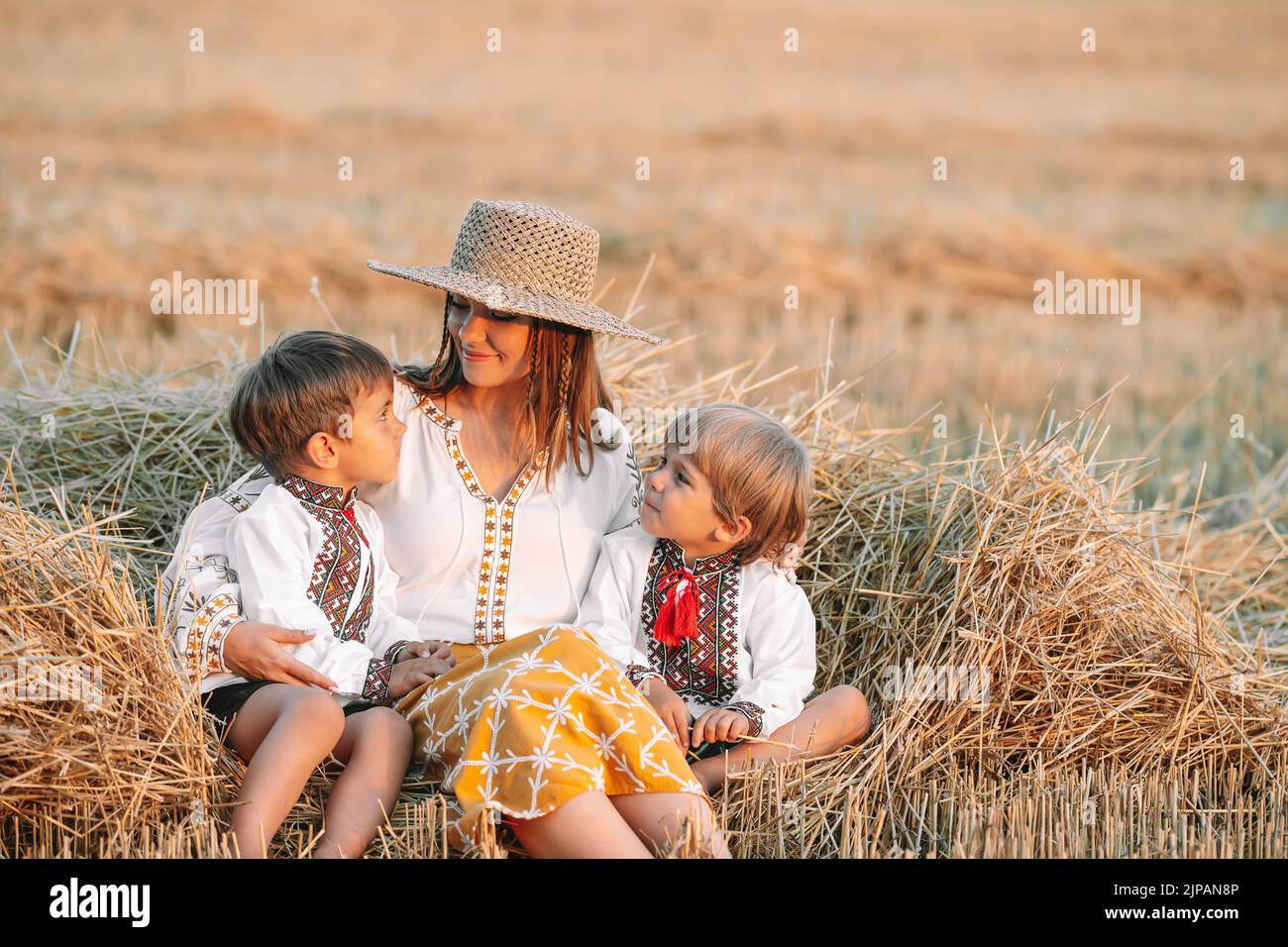 Ukrainische Jungen und Mutter sitzen nach der Ernte auf dem Weizenfeld zusammen. Familie ...