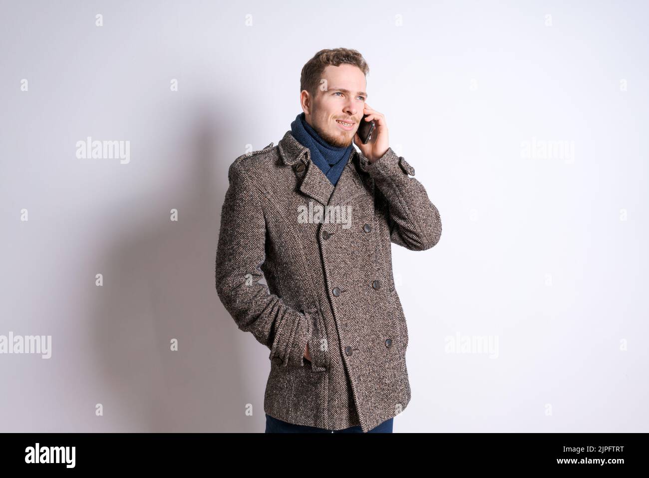 Der junge Kaukasusmann trägt einen modischen langen Mantel mit Schal ...