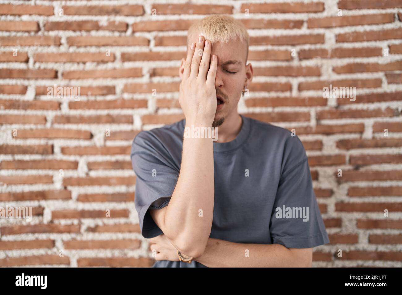 Junger kaukasischer Mann, der über einer Ziegelwand gähnend müde steht ...