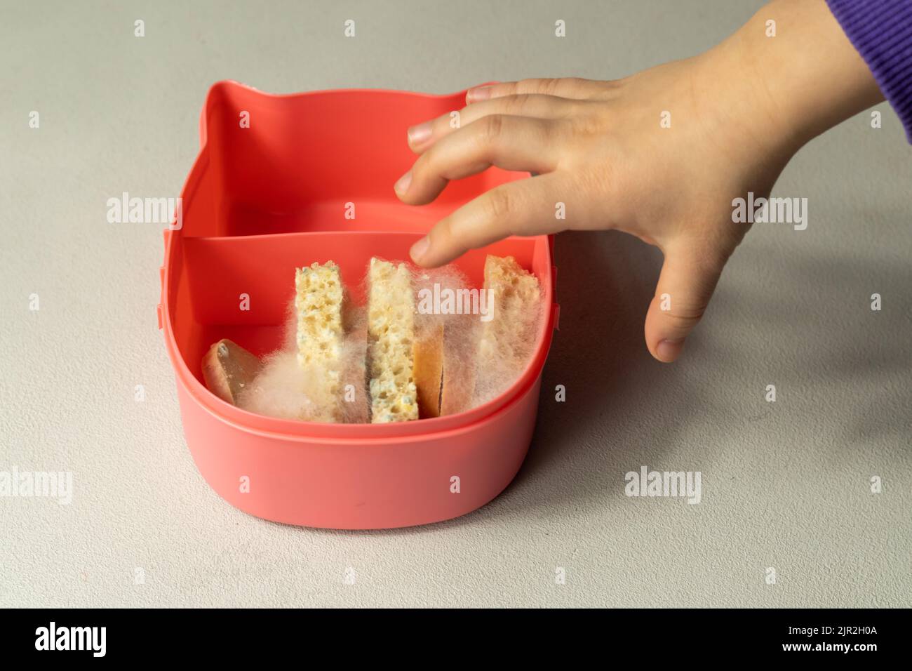 Eine Kinderhand greift nach einer Lunchbox mit Brotscheiben und Wurst ...