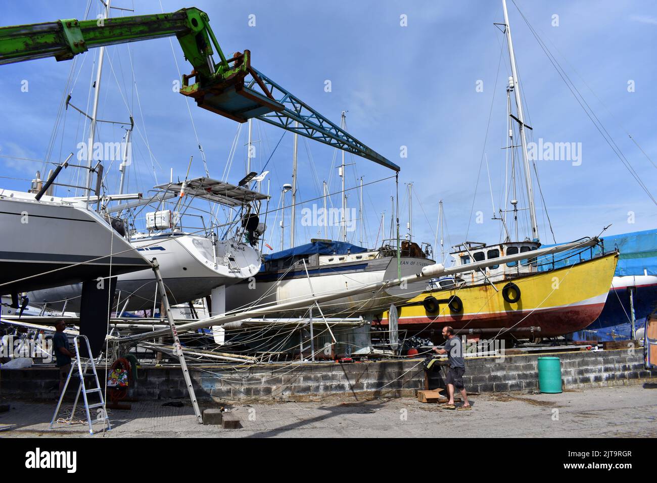 Kran, der einen Mast wieder auf ein Segelboot in East Llanion boatyard ...