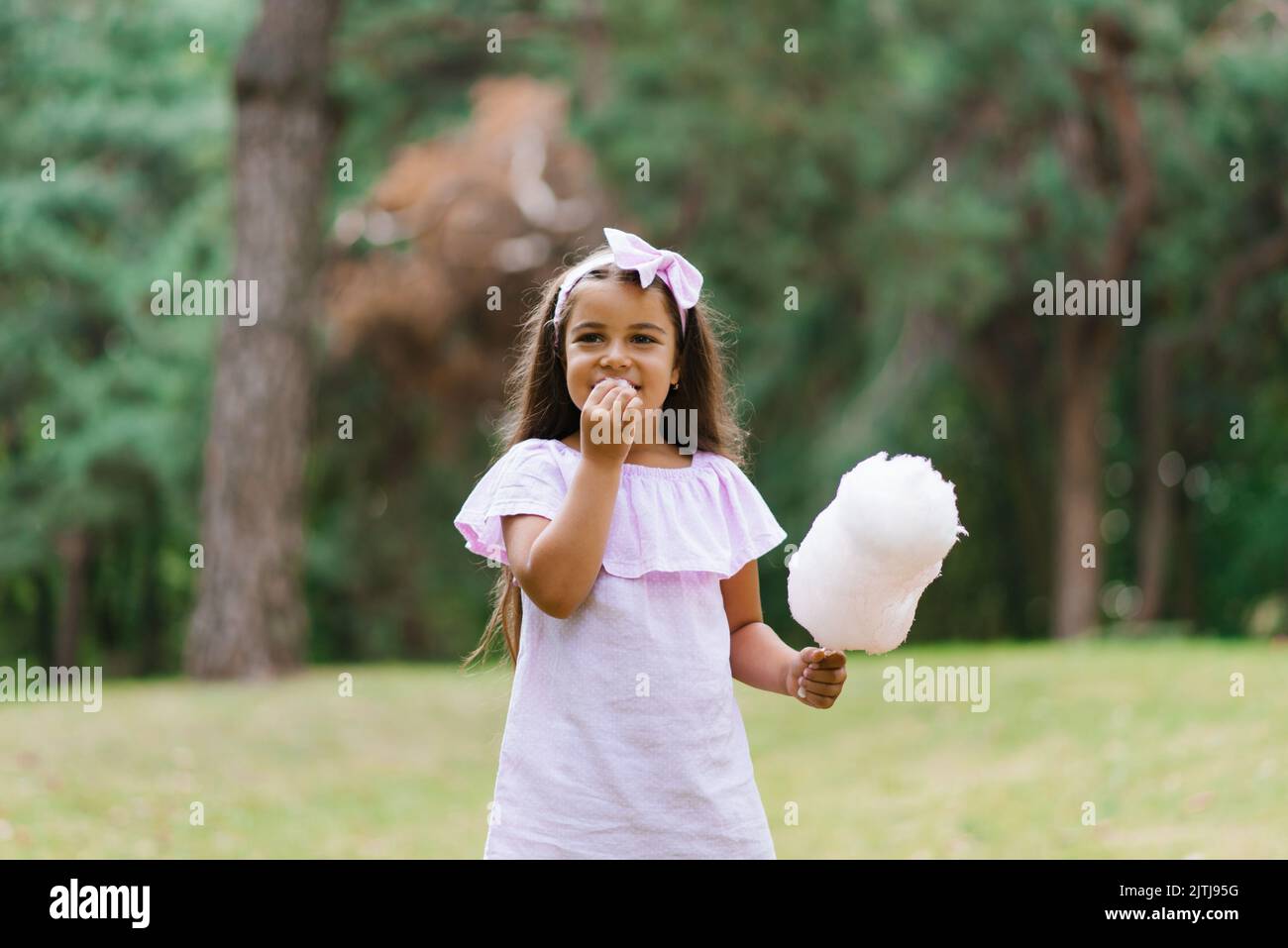 Mädchen in einem Vergnügungspark im Sommer isst Zuckerwatte und lächelt ...