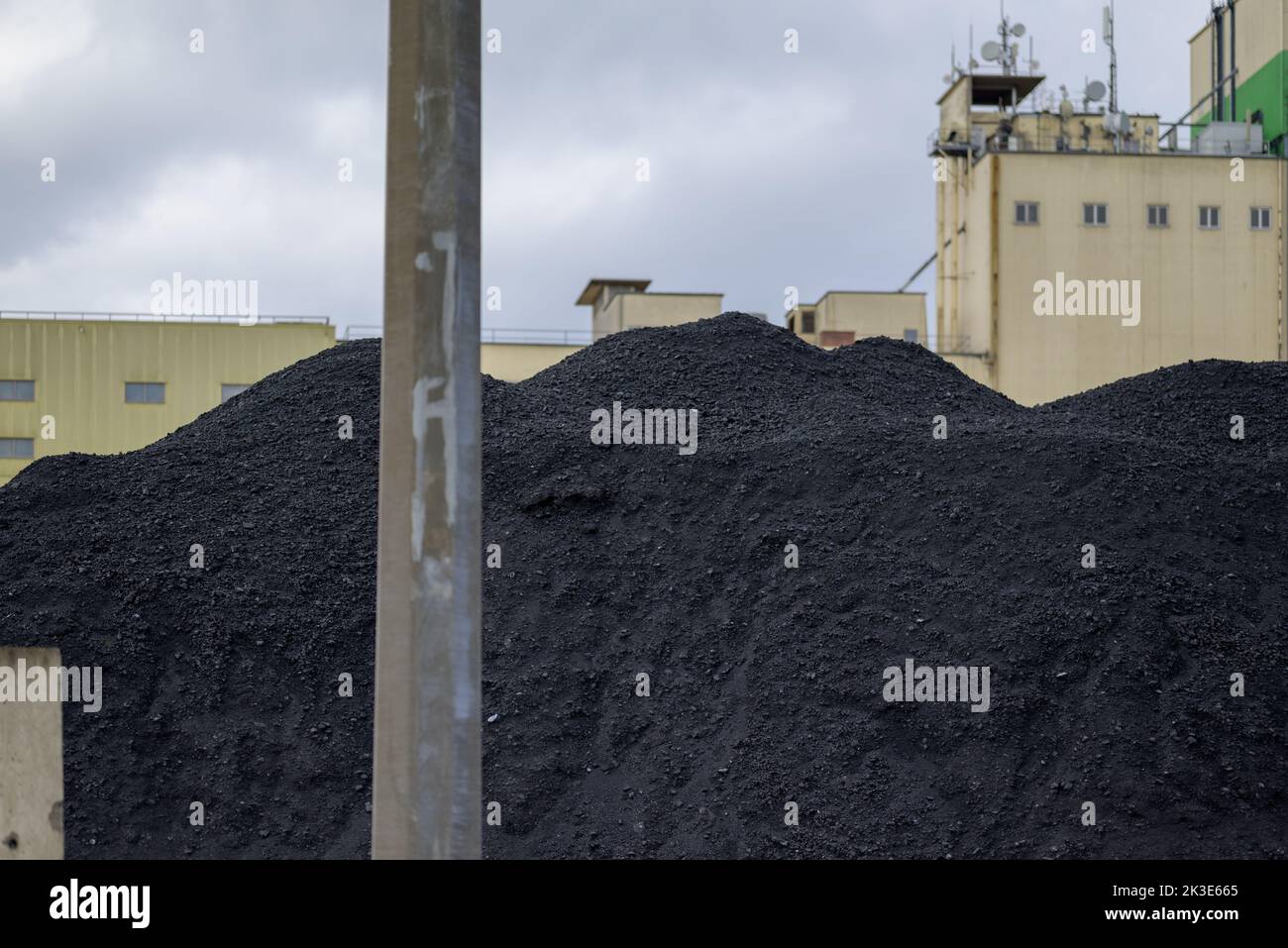 Riesiger Berg aus Steinkohle und im Hintergrund ein Industriegebäude in ...