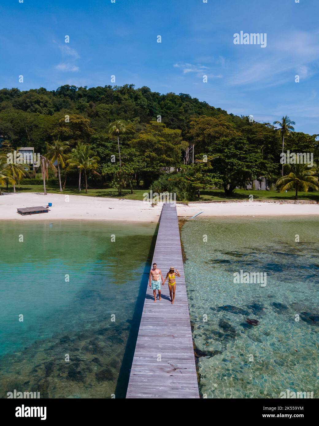 Ein Paar Männer und Frauen auf einem Holzbrett Spaziergang auf einer tropischen Insel in ...