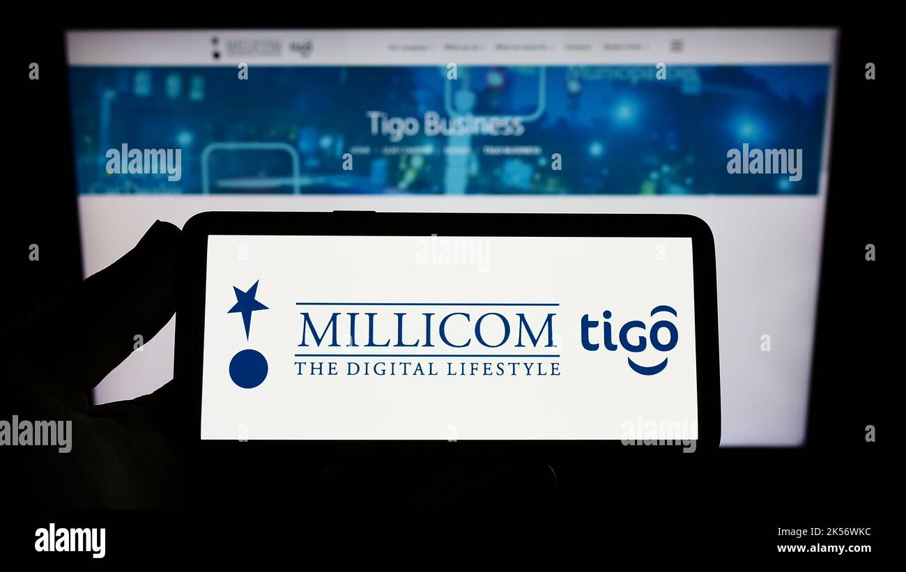 Person, die das Smartphone mit dem Logo der Firma Millicom ...