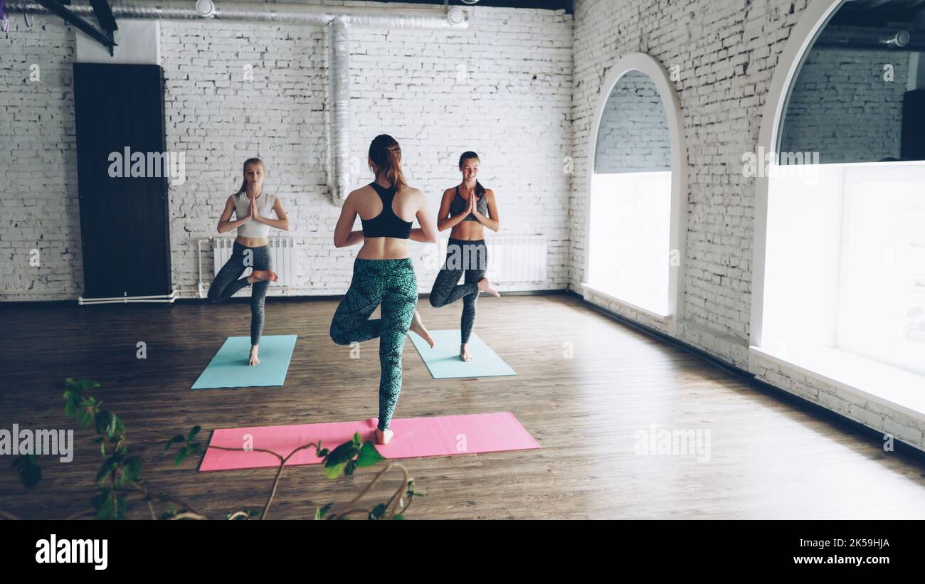 Eine erfahrene Yogalehrerin zeigt zwei attraktiven Schülerinnen beim Gruppentraining im ...