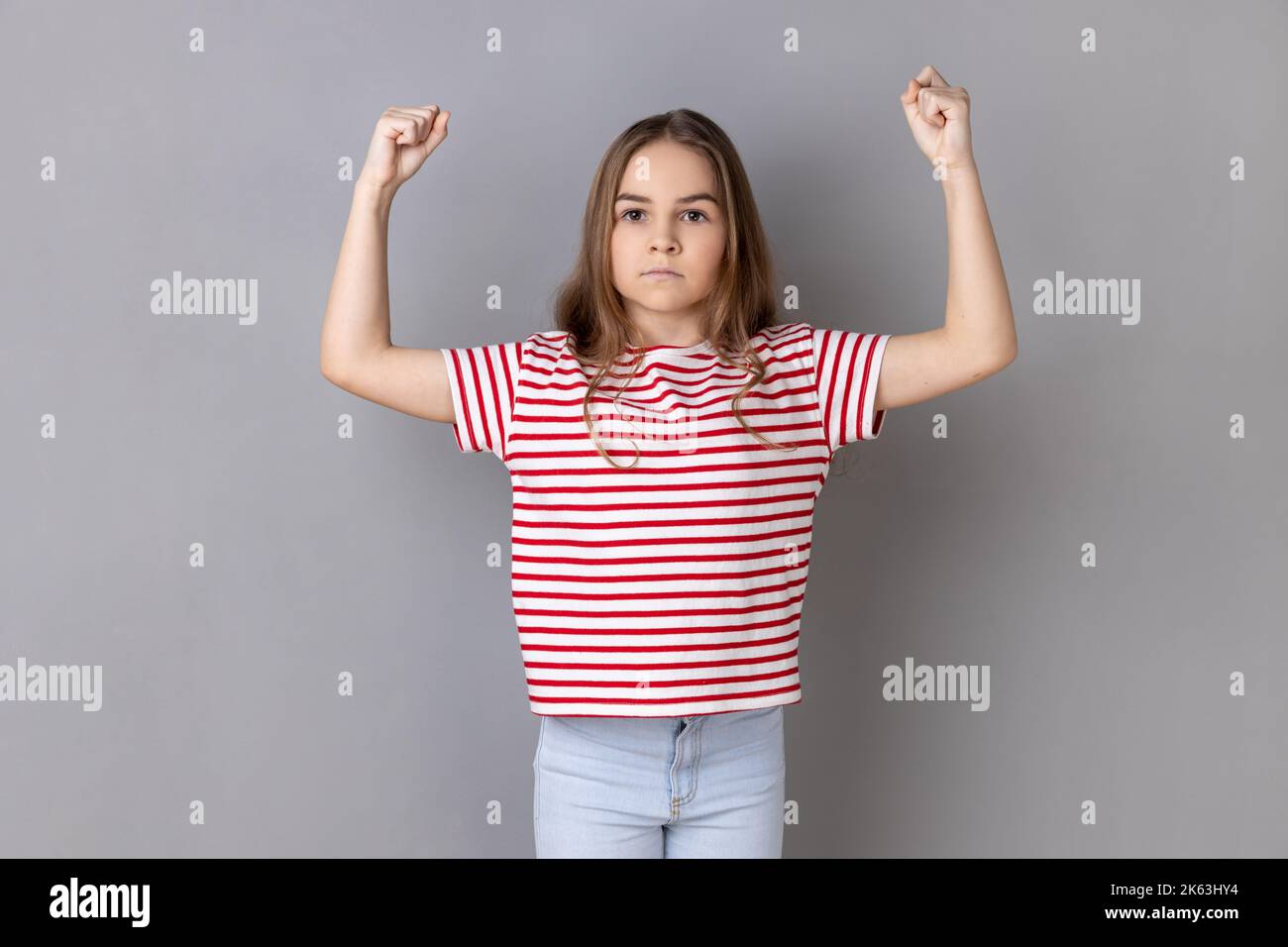 Ein starkes, dunkelhaariges kleines Mädchen, das gestreiftes T-Shirt ...