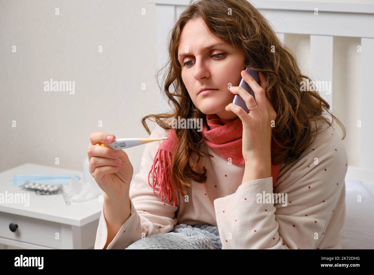 Kranke Frau ruft den Arzt am Telefon mit einem Thermometer in der Hand ...