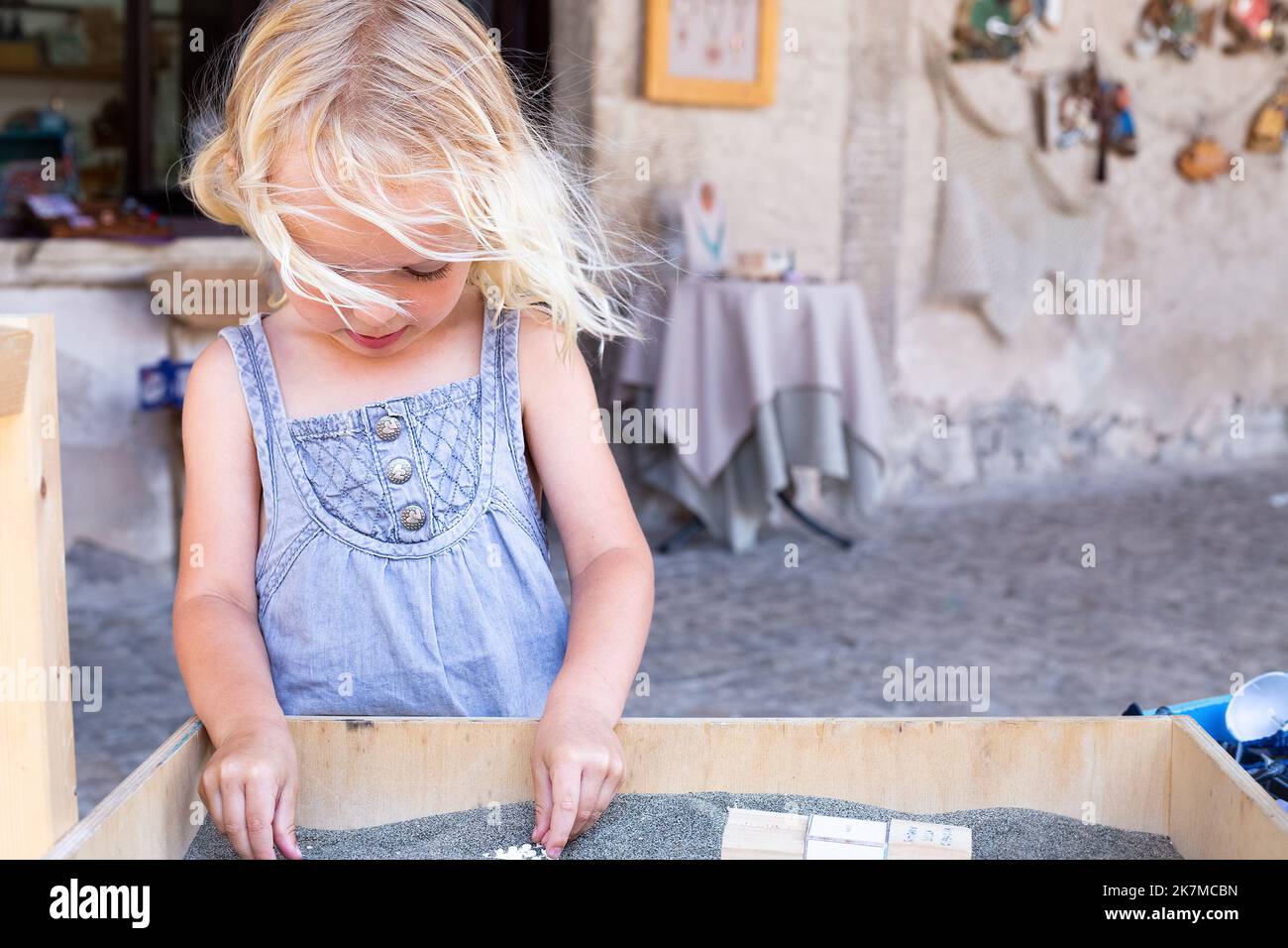 Blonde Mädchen konzentriert sich auf das Spielen mit Sand auf dem Tisch ...