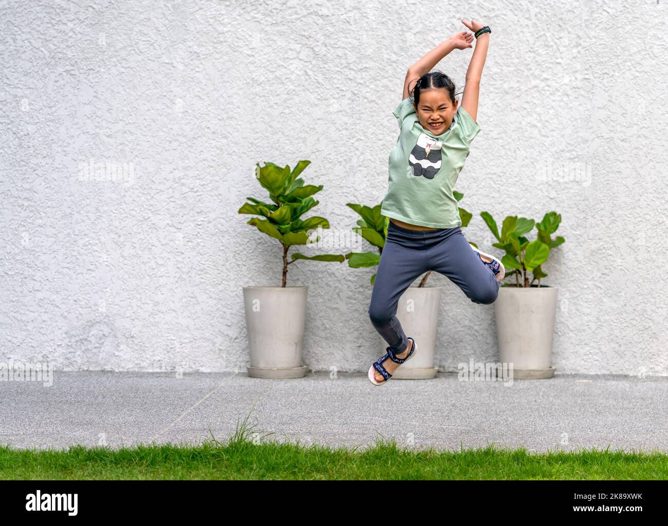 Glückliches asiatisches Kind springt in einer Pose in einem Garten des ... Glückliches asiatisches Kind springt in einer Pose in einem Garten des ...