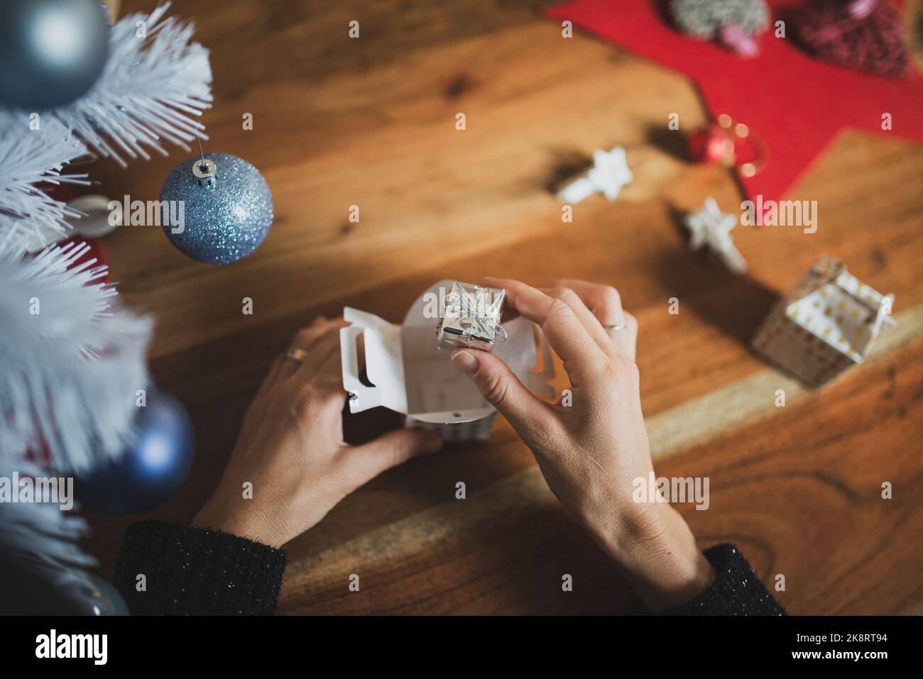 Draufsicht auf weibliche Hände, die neben einem weißen weihnachtsbaum mit blauen ...