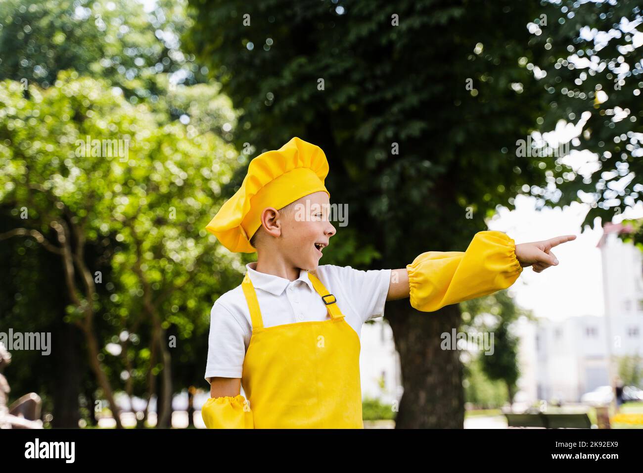 Zeigen Sie nach rechts. Schöner Koch Kind in gelben Köchhut und Schürze ...