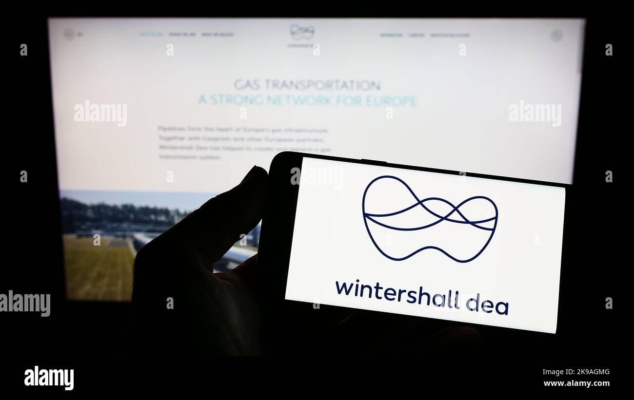 Person mit Mobiltelefon und Logo des deutschen Öl- und Gasunternehmens ...