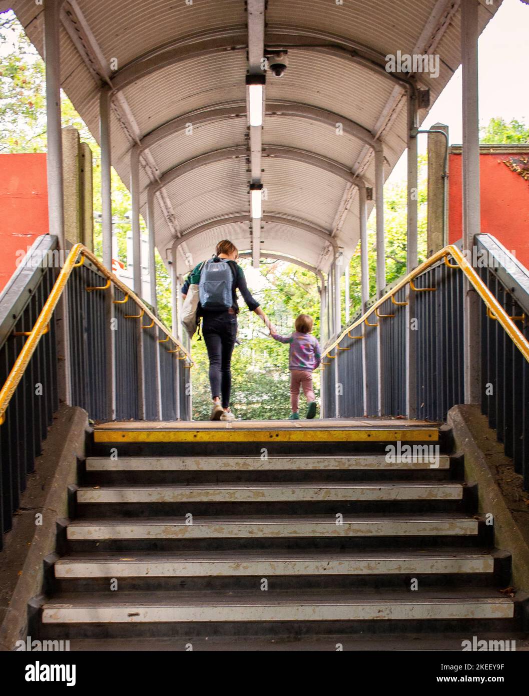 Mutter und kleines Kind halten sich die Hände und gehen entlang des Durchgangs zur U-Bahn ...