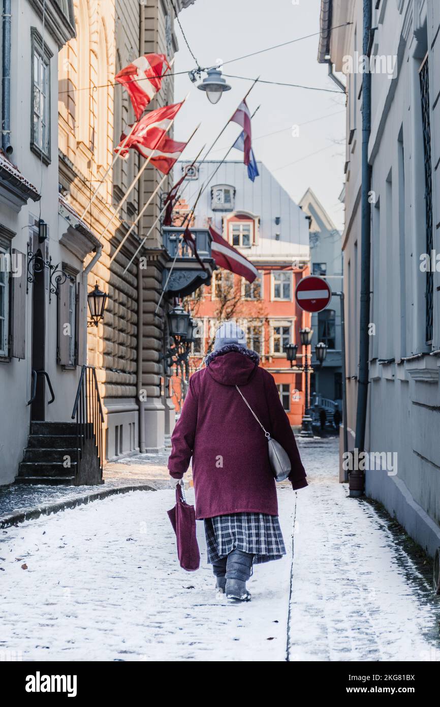 Riga, Lettland - November 20 2022: Ältere Frau in Winterkleidung, die ... Riga, Lettland - November 20 2022: Ältere Frau in Winterkleidung, die ...