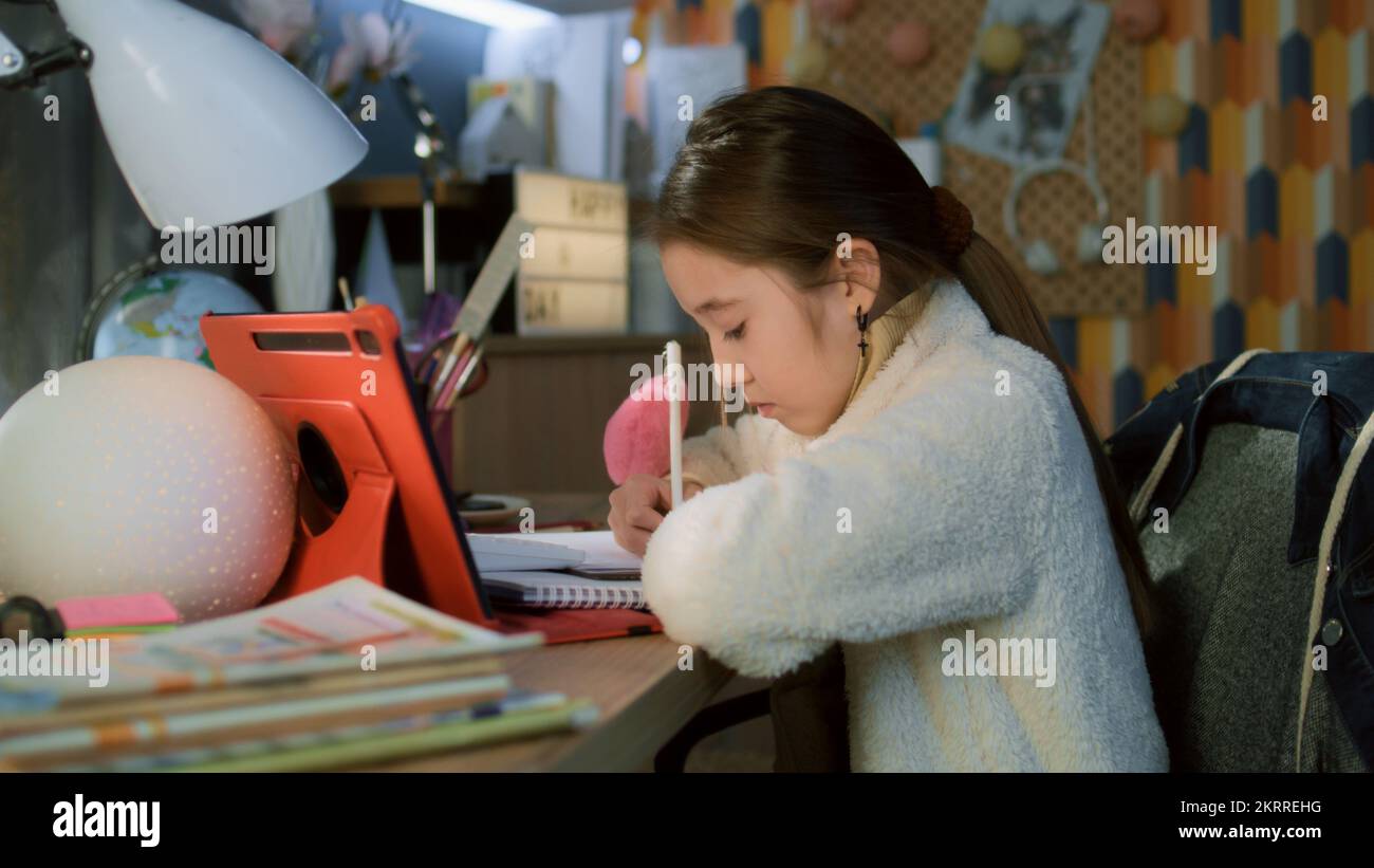 Junge Asiatin sitzt zu Hause am Tisch und spricht mit der Lehrerin. Der ... Junge Asiatin sitzt zu Hause am Tisch und spricht mit der Lehrerin. Der ...