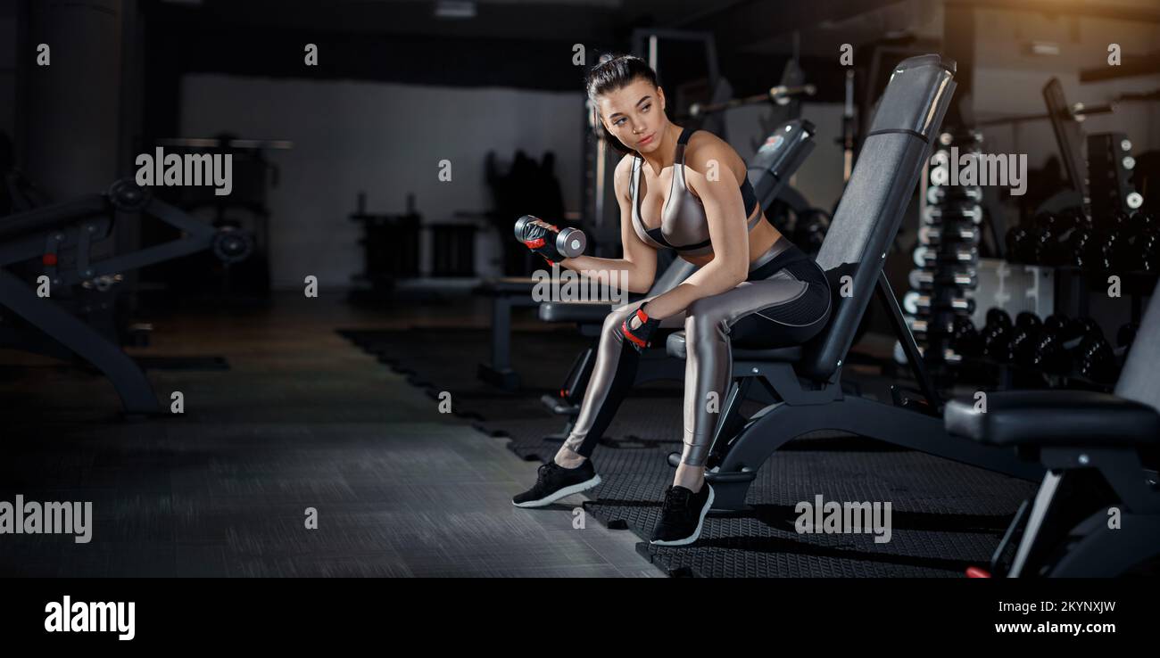 Schlankes Bodybuilder-Mädchen, hebt schwere Kurzhanteln, steht vor dem ...