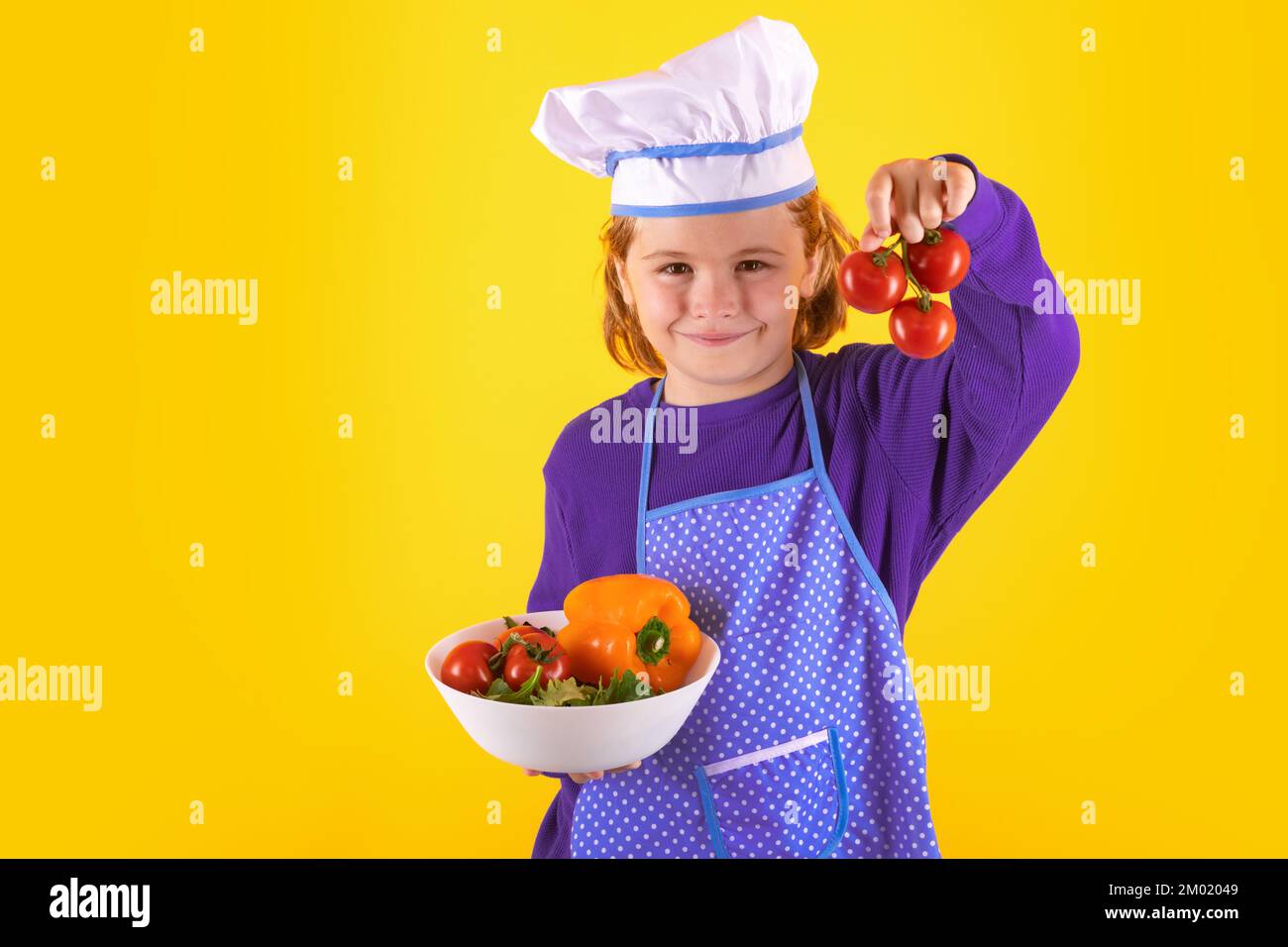 Kinderkoch hält Tomate. Das Porträt des kleinen Kindes in der Uniform ...