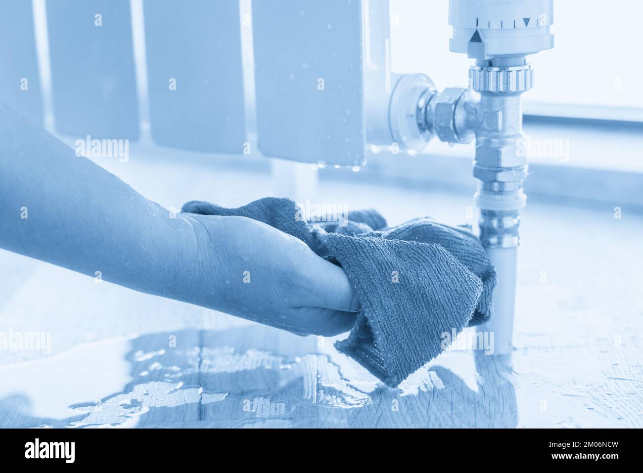 Weibliche Hand mit einem Lappen, der das Wasser vom Heizkörperleck ...