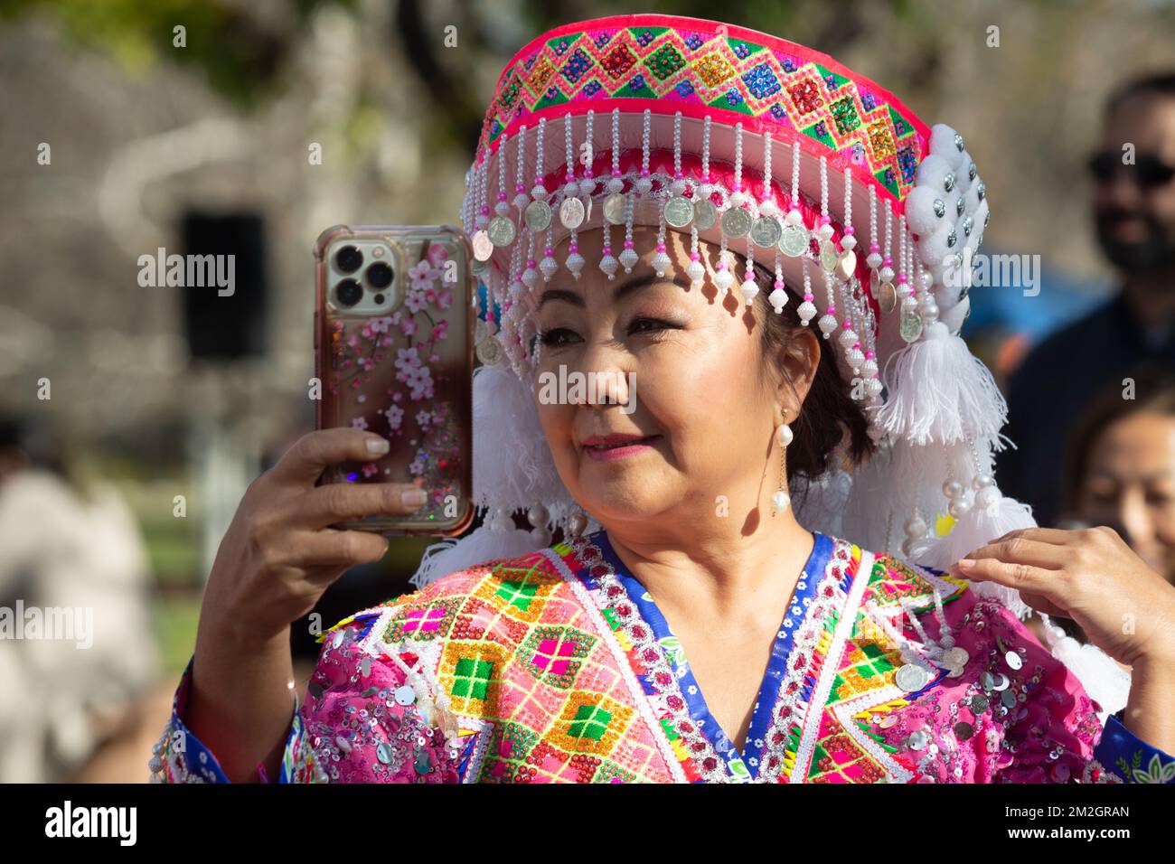 A woman in traditional Hmong attire takes a photo with a cell phone at ...
