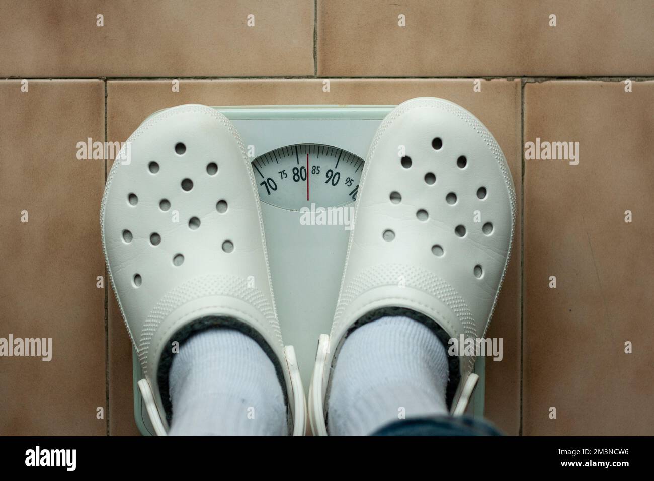 Analoge Waage, auf der eine Person gewogen wird und deren Gewicht in kg ...