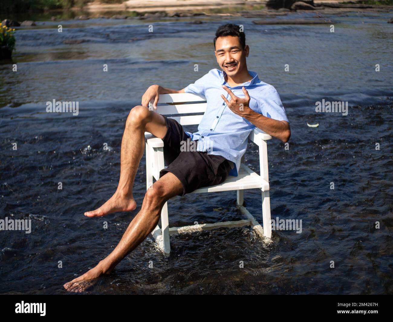 Ein Mann, der in einem Stuhl mitten im Fluss im Café namens „Nature Park“, Wong Thong ...