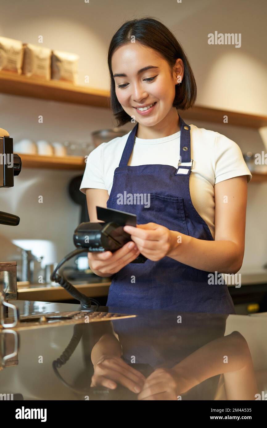 Ein wunderschönes lächelndes asiatisches Mädchen, der Barista legt die ...