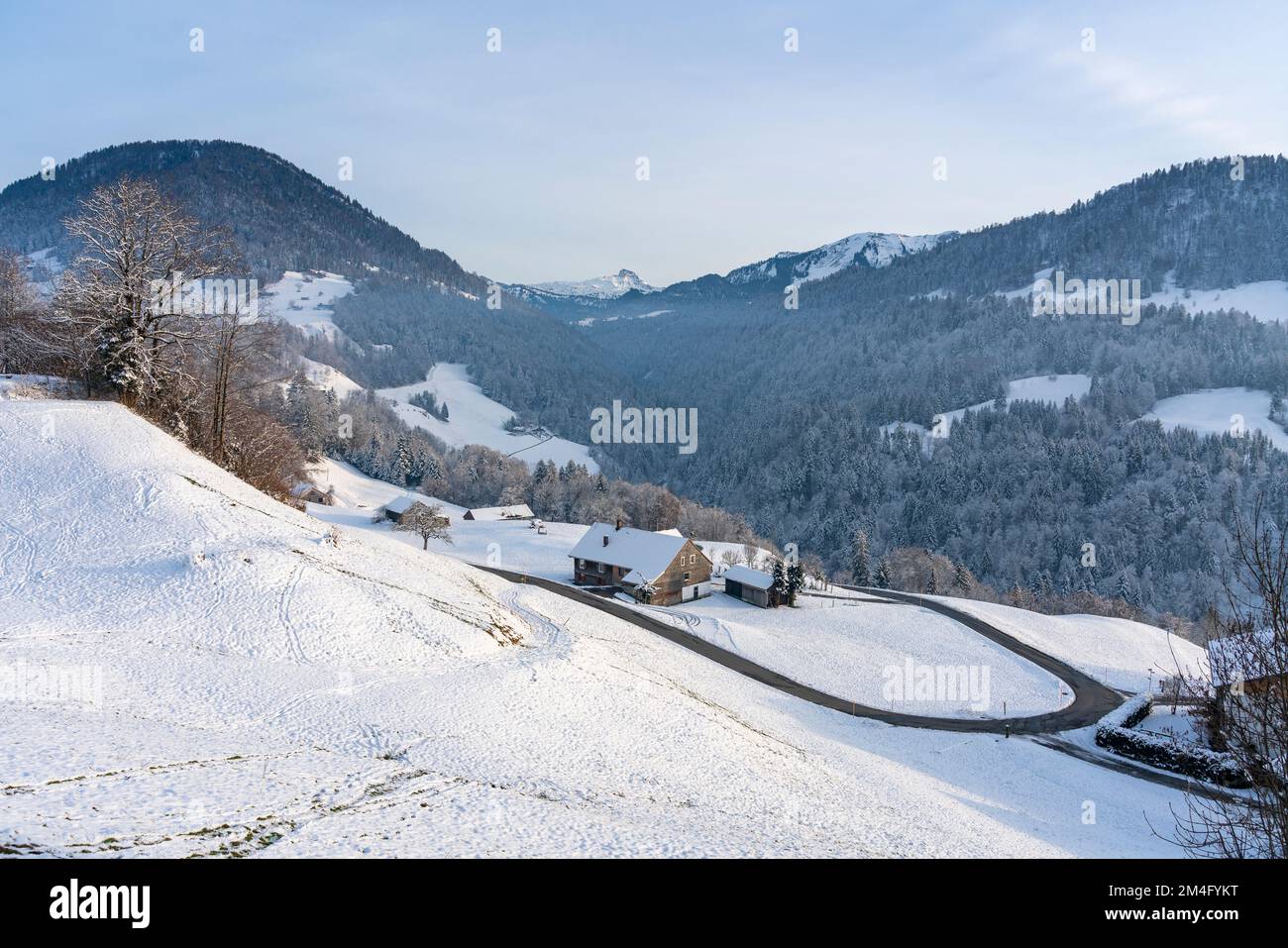 Frisch verschneite Bergstraße, die sich ins Tal schlängelt, Bauernhaus ...