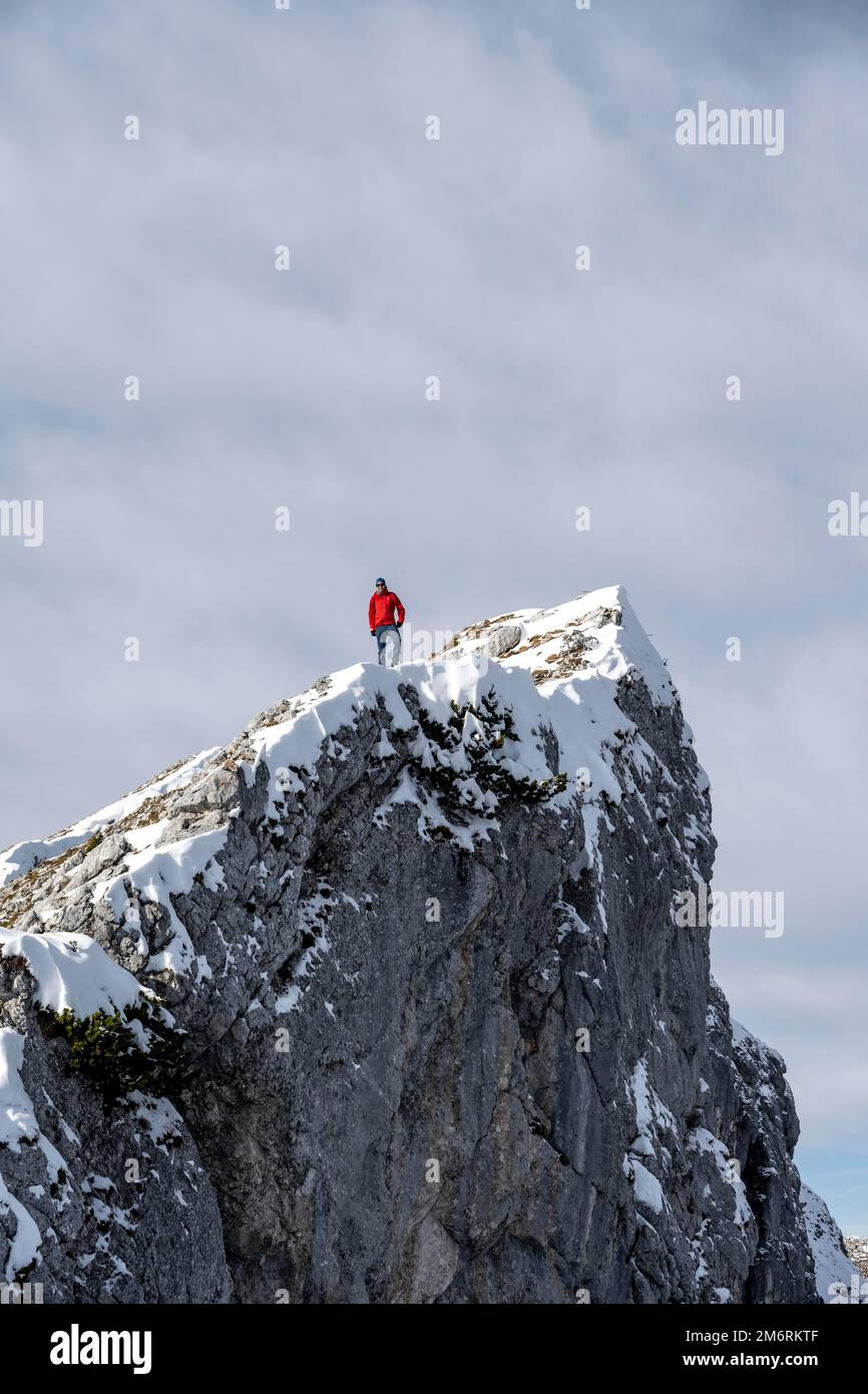 Bergsteiger mit roter Jacke auf einem Felsturm, Berge im Winter mit ...