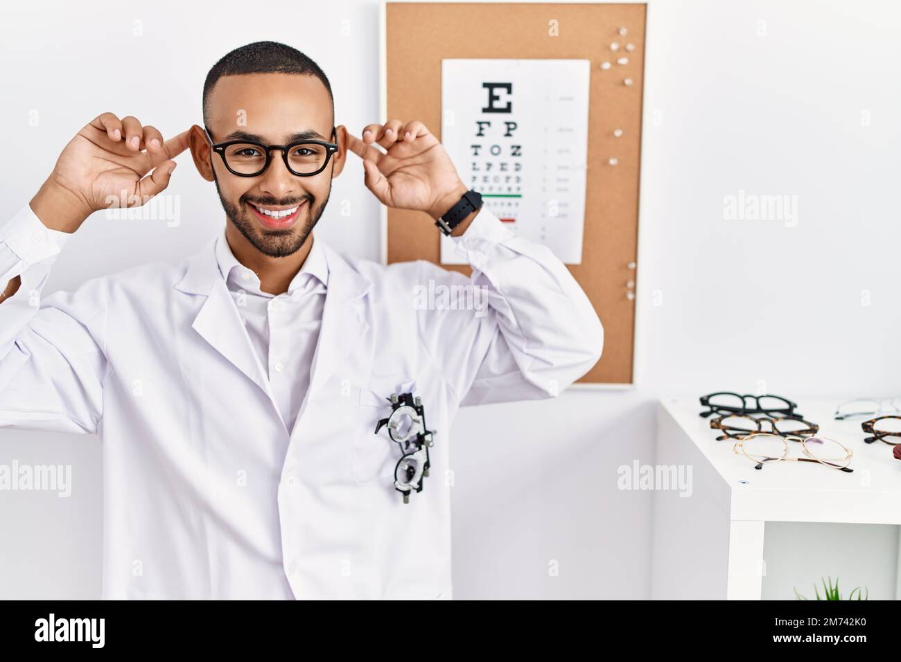 Ein afroamerikanischer Optiker, der beim Sehtest steht, lächelt mit den ...