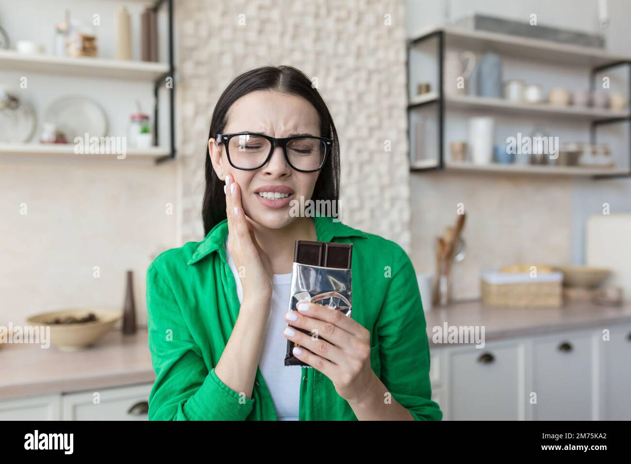 Eine junge Frau sitzt in der Küche am Tisch zu Hause und isst eine ...