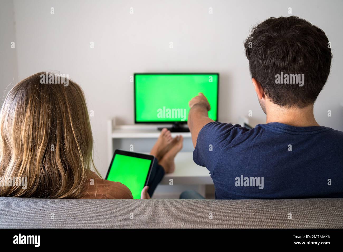 Das junge Paar sitzt zu Hause mit einem Tablet auf der Couch. Grüner ...