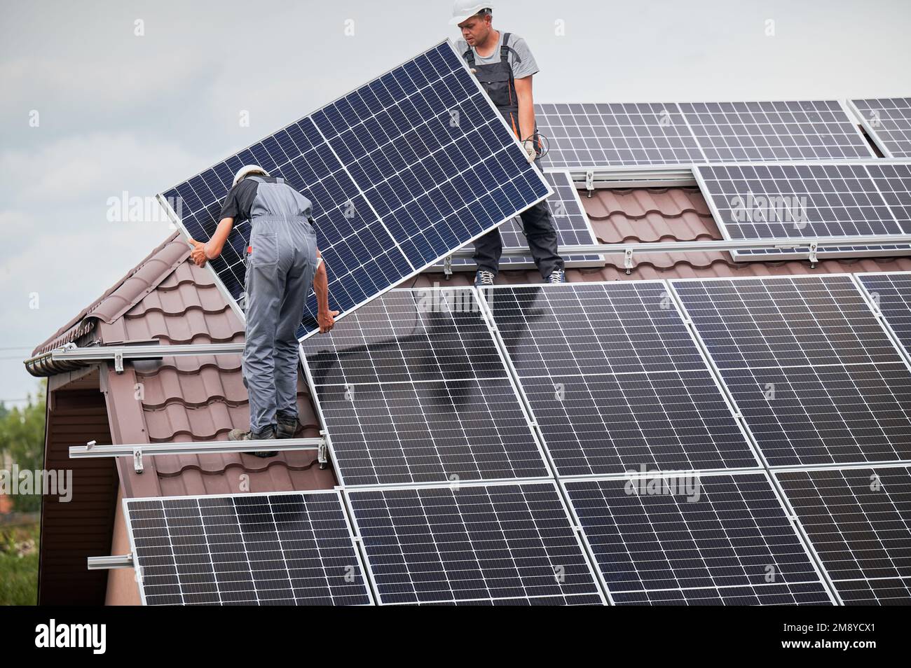 Männer, Arbeiter, die Photovoltaik-Solarmodule auf dem Dach des Hauses ...