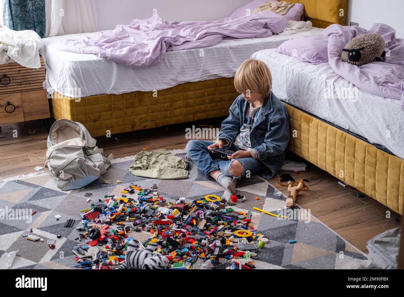 Ein Junge, der sein Handy benutzt, in einem dreckigen Kinderzimmer ...