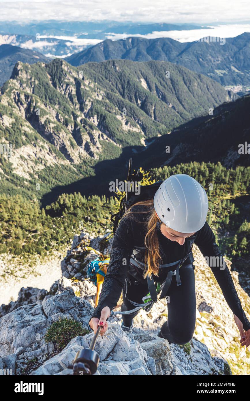 Vertikales Foto einer Bergsteigerin mit weißem Helm, der nach unten ...