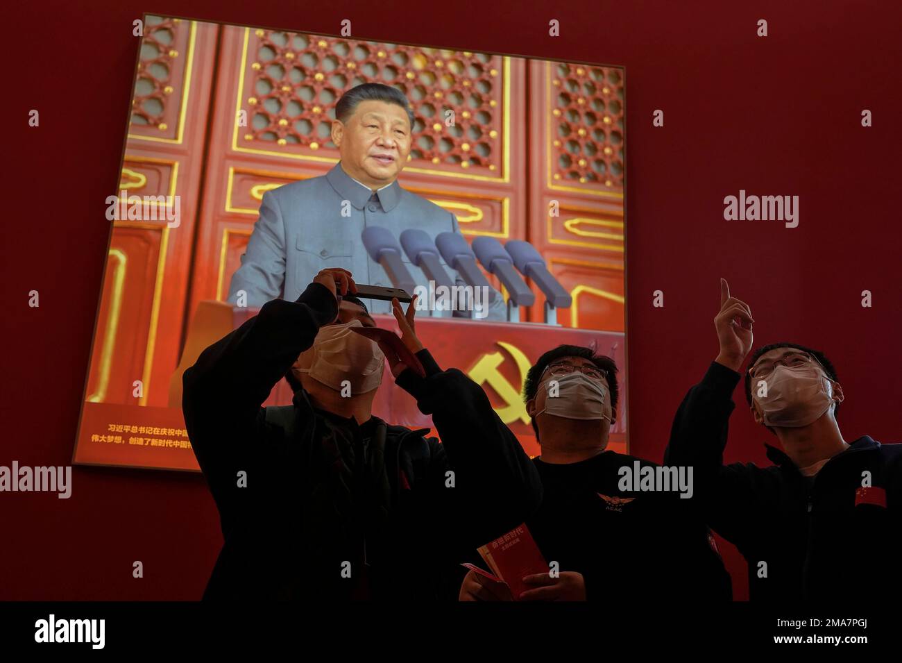 FILE- Visitors wearing face masks stand watch in front of a screen ...